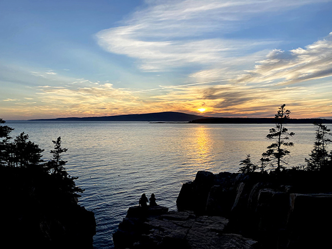 Silhouettes at sunset capture that perfect Maine moment &ndash; two figures pausing to absorb nature's nightly color explosion.
