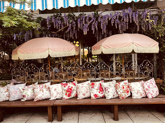 A bench paradise of floral pillows under pink umbrellas. The only thing missing is someone reading poetry aloud while you wait for your table.
