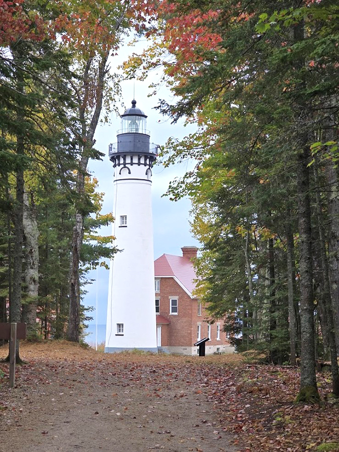 Au Sable Light Station stands sentinel among fall foliage, its white tower a beacon of human perseverance amid nature's seasonal art show.