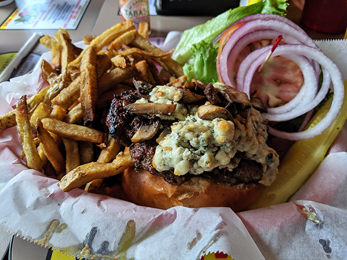 Blue cheese and saut&eacute;ed mushrooms crown this burger masterpiece &ndash; crispy fries standing at attention, ready for their supporting role.