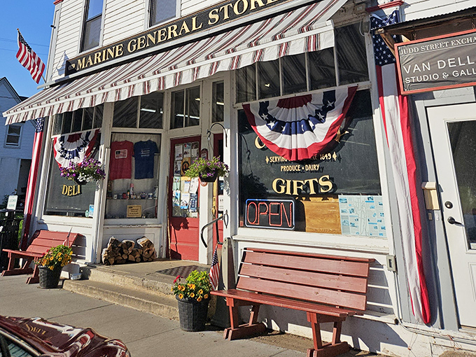 The storefront wears its patriotic bunting with pride, flanked by flowers and benches that invite lingering while you contemplate which pastry justified this entire trip.