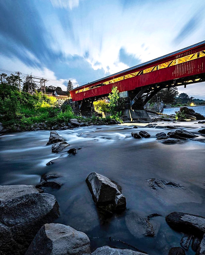 Taftsville Covered Bridge glows red against autumn foliage &ndash; engineering marvel meets artistic masterpiece in typical Vermont fashion.