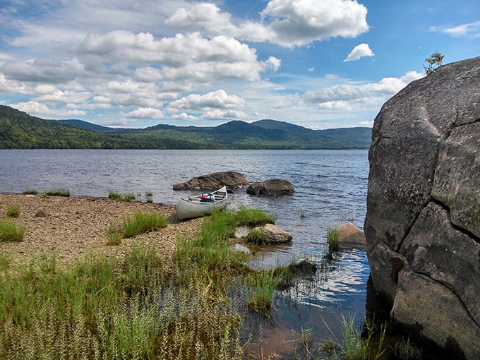 Aziscohos Lake's pristine shoreline welcomes a lone canoe, with mountains creating a perfect backdrop for wilderness swimming adventures.