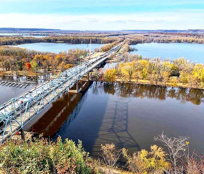 The mighty Mississippi flows beneath Barn Bluff's iron bridge, autumn colors painting the shoreline in fiery hues.