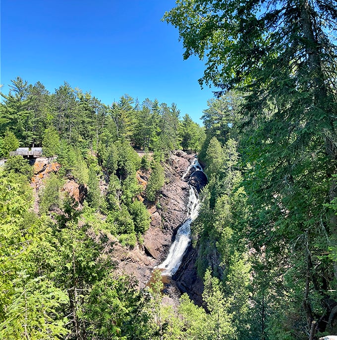 Big Manitou Falls cascades dramatically through a forest canyon, its white waters standing out against the rugged rock face and surrounding greenery.