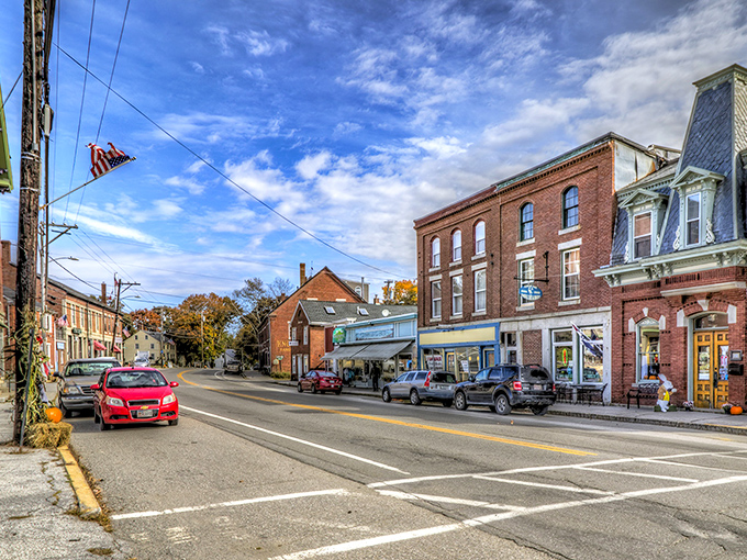Searsport's Main Street showcases classic New England brick architecture, with historic storefronts lining the road under a brilliant blue sky.
