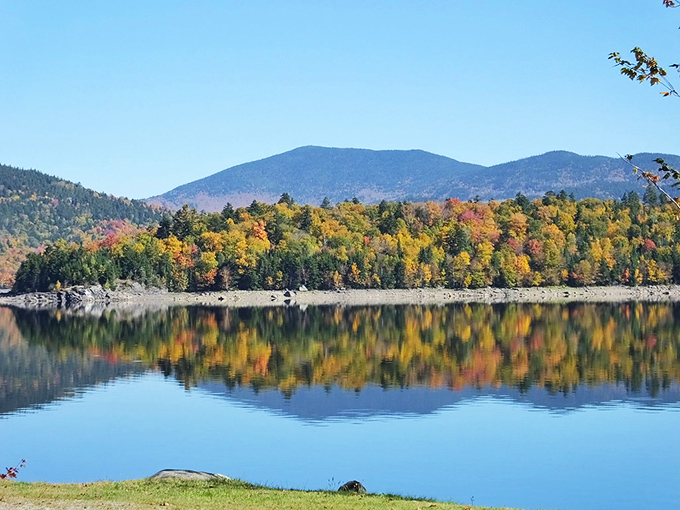 Fall foliage creates a mirror image on Aziscohos Lake's glass-like surface &ndash; nature's own infinity pool nestled in Maine's western mountains.