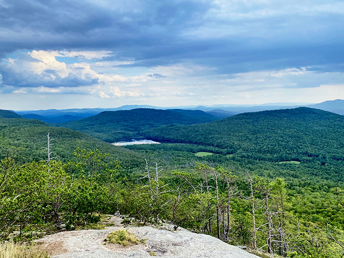 The view from Blueberry Mountain stretches for miles across Maine's western mountains, with a pristine lake nestled among endless forest.
