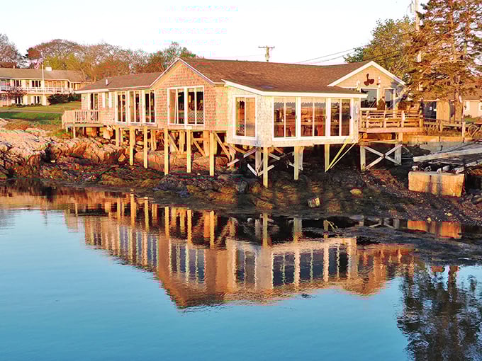 Waterfront homes perched on stilts reflect in the glassy morning waters of Harpswell, where Maine's coastal living balances precariously between land and sea.