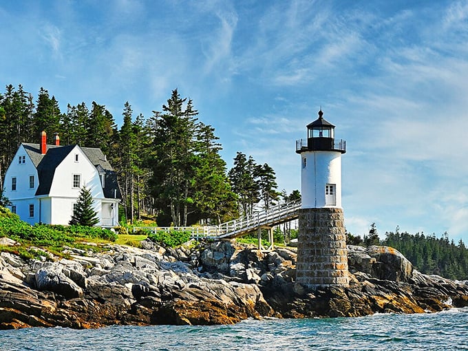 The classic white keeper's house and lighthouse create that quintessential Maine coastal image against a backdrop of spruce trees and Atlantic blue.