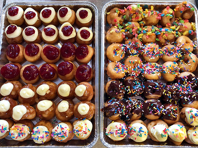 Trays of colorful mini donuts glisten with toppings &ndash; some with fruit filling, others with cream, and many with rainbow sprinkles. Tiny circles of joy!