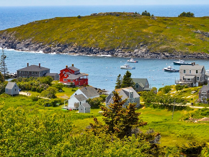 Colorful houses dot the hillside of Monhegan Island, with the bright red building standing out against the blue harbor where fishing boats gently bob.