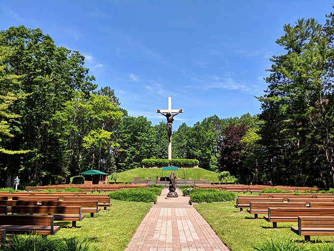 The towering crucifix rises majestically against a brilliant blue sky, drawing visitors from the highway into this unexpected woodland sanctuary.
