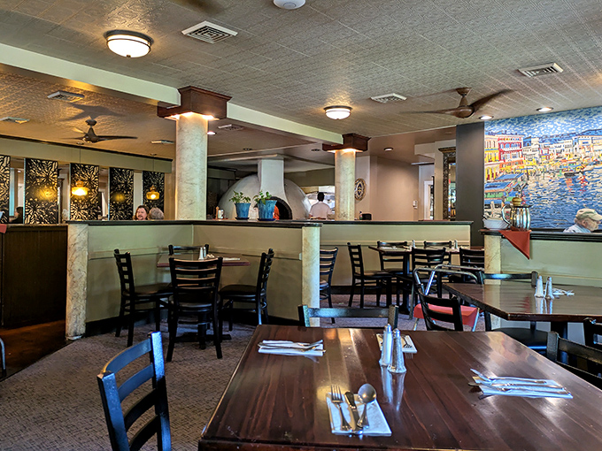 The dining room balances elegance with comfort &ndash; white tablecloths meet rustic beams while the open kitchen buzzes with culinary energy.