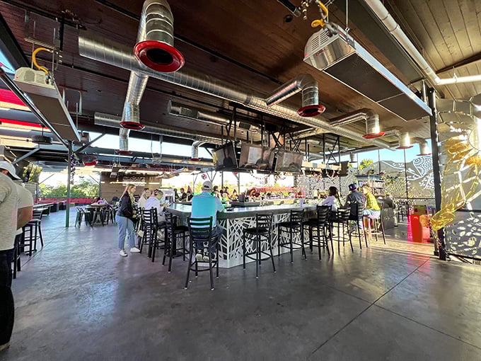 Industrial-chic meets brewery functionality at The Perch's indoor bar, where exposed ductwork hovers above a bustling communal atmosphere.
