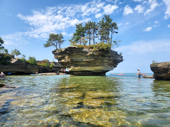 Adventurous kayakers circle the geological marvel, providing scale to this mushroom-shaped wonder that seems almost too whimsical to be real.