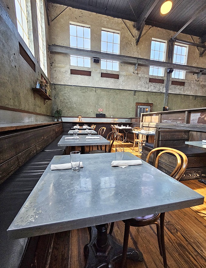 Sunlight streams through towering windows, illuminating concrete walls and wooden beams that whisper stories from the building's ice-making past.