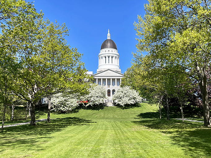 Maine's State House rises majestically above Capitol Park's manicured lawns, its white dome gleaming like a beacon against the clear blue sky.