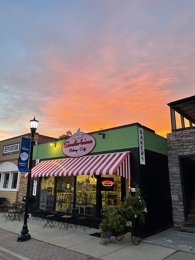Sweetie-licious Bakery Cafe glows under a sunset sky, its candy-striped awning beckoning dessert lovers like a beacon of sweetness.