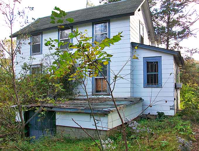 The old shop's porch sags with stories untold, its weathered boards and empty windows hinting at busy days long gone.