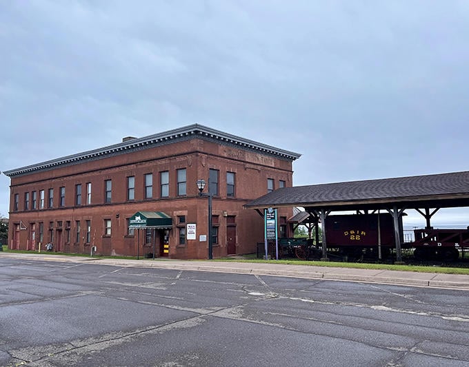 The historic red brick depot in Two Harbors houses the Lake County Historical Society, with vintage train cars displayed under the protective wooden shelter.
