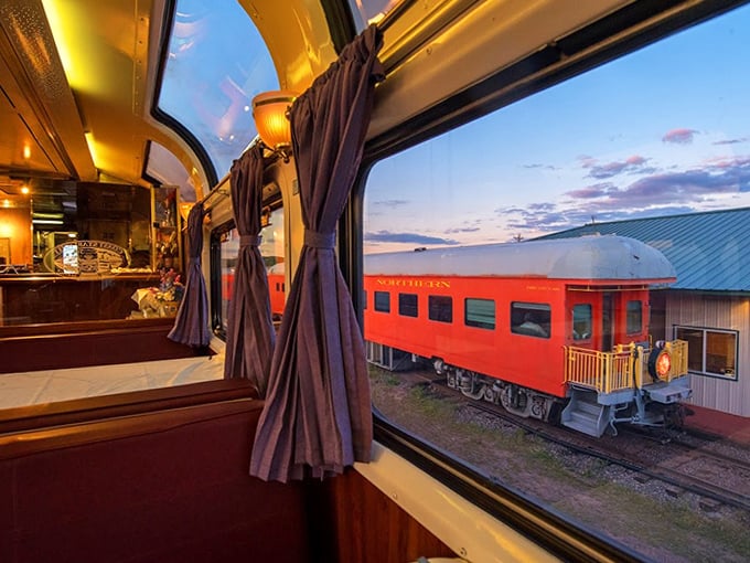 Through velvet curtains, a neighboring car glows red against the twilight sky &ndash; railroad romance captured in a single frame.