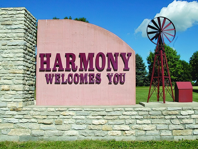 The "Harmony Welcomes You" sign, with its cheerful pink backdrop and windmill silhouette, promises visitors the warm embrace of small-town hospitality.
