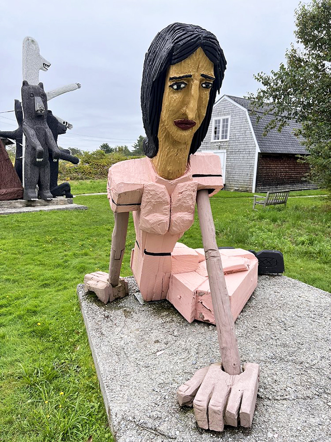 This carved wooden woman in pink attire sits contemplatively on her concrete perch, her elongated features suggesting both strength and vulnerability.