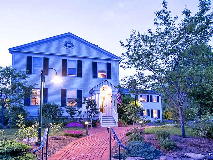 This stately white colonial inn glows with welcoming light at dusk, promising elegant dining and gracious Vermont hospitality inside.