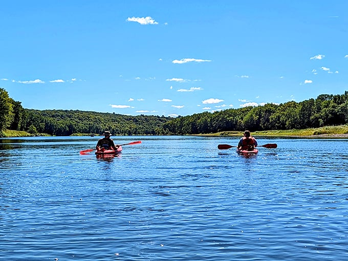 Kayakers glide across the glassy surface of the St. Croix River, their colorful boats adding the only ripples to this perfect mirror of blue sky and green hills.