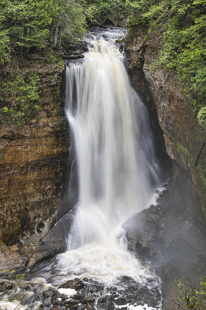 The forest parts to reveal Miners Falls, where crystal clear water crashes into a blue-green pool nestled between towering pines.
