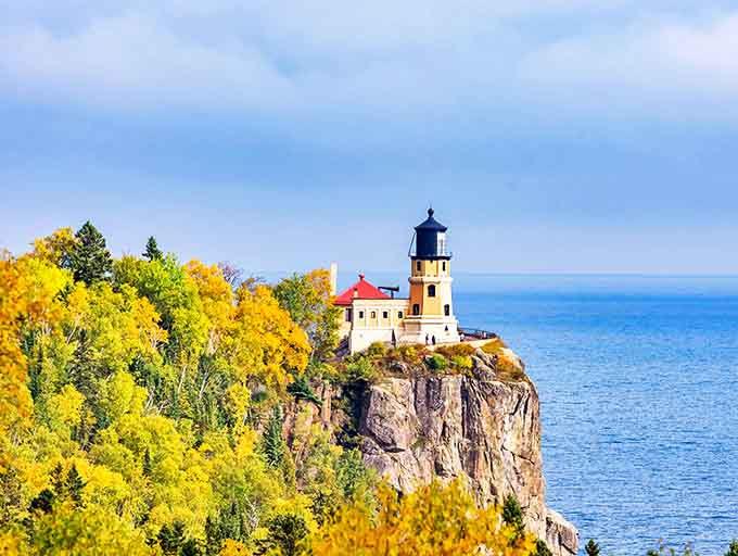 Fall colors frame this iconic lighthouse against dramatic cliffs, creating Minnesota's most photographed scene as golden leaves complement the historic structure.