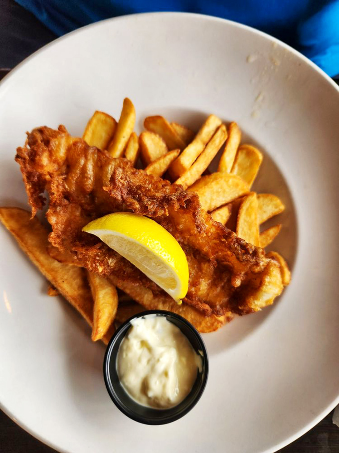 Golden-battered fish rests atop a mountain of crispy fries, accompanied by a wedge of lemon and creamy dipping sauce – simple perfection.