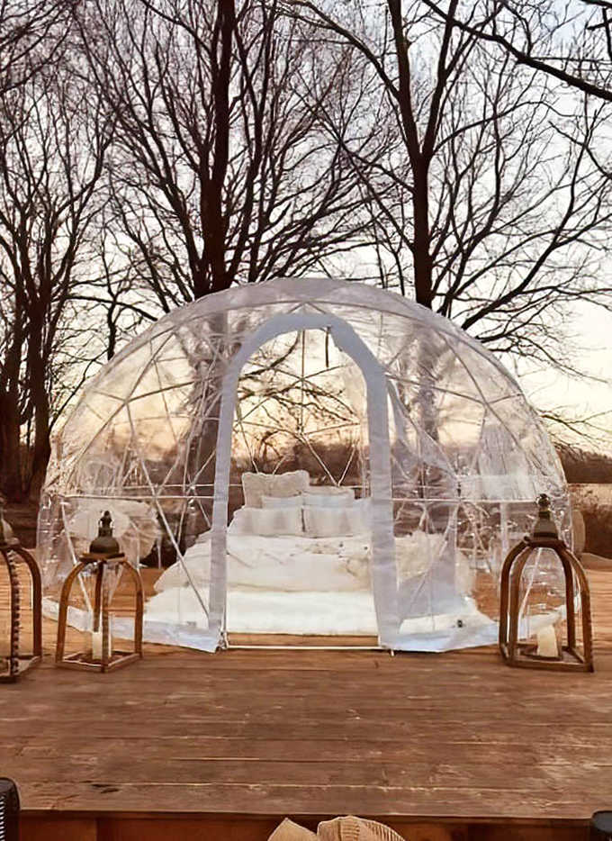 Daylight reveals the dome's perfect integration with nature, perched on a wooden deck with rustic lanterns standing guard.