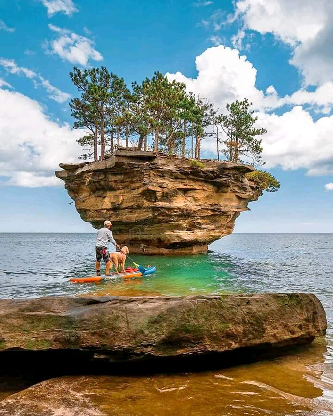 A paddleboarder glides through turquoise waters toward Turnip Rock, demonstrating why this hidden gem deserves a spot on every Michigan bucket list.
