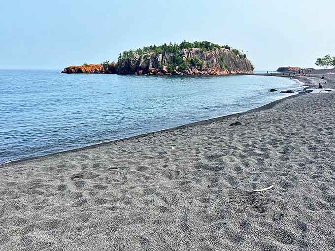 Black Beach's unique shoreline stretches toward a rocky outcropping, where dark pebbles meet the crystal-clear waters of Lake Superior.