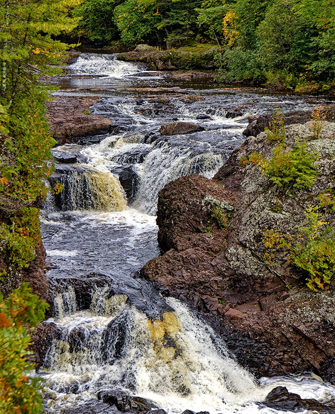 Potato River Falls rushes through a rocky gorge, its powerful waters carving through stone as sunlight filters through the surrounding pine forest.