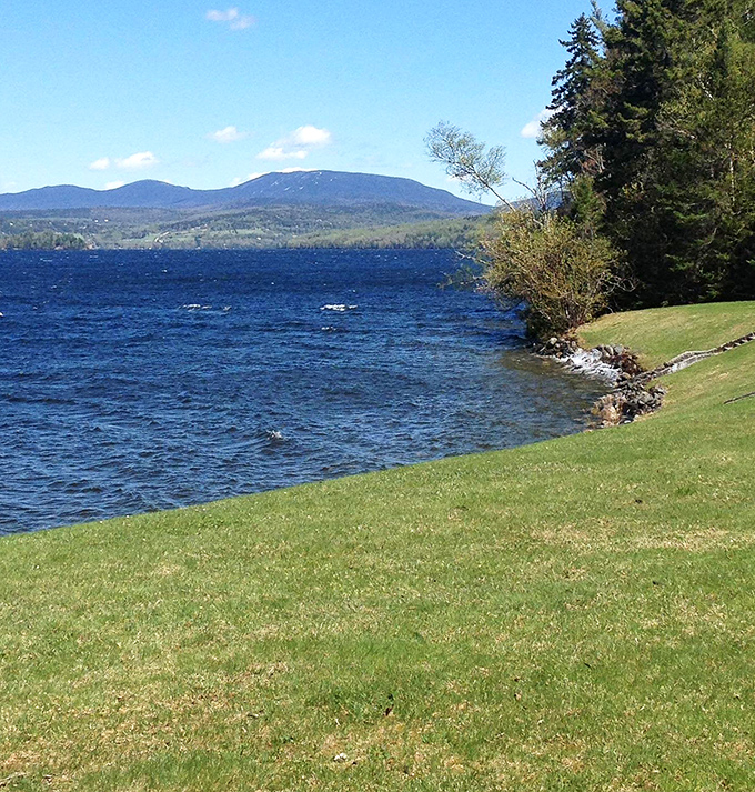 The shoreline of Rangeley Lake invites visitors to dip their toes where forest meets water, with Mount Saddleback standing guard in the distance.