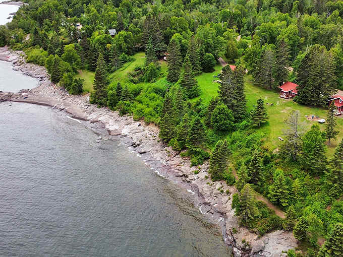 The rocky shoreline near Schroeder reveals Lake Superior's crystal-clear waters, with the town's harbor visible in the distance under blue summer skies.