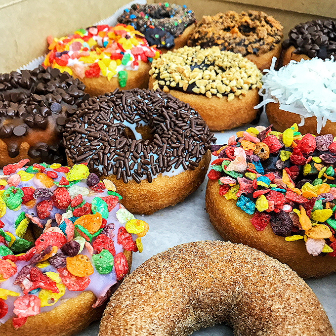 A colorful array of custom donuts with every topping imaginable &ndash; from fruity pebbles to coconut flakes &ndash; each one a unique sugary experiment.