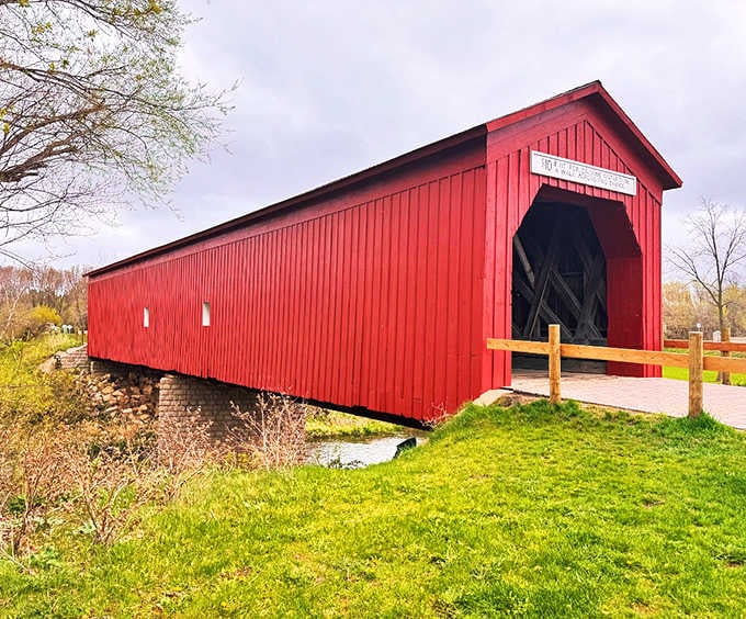 Stretching across its waterway, the Zumbrota Covered Bridge's classic red siding creates a striking contrast against green surroundings.