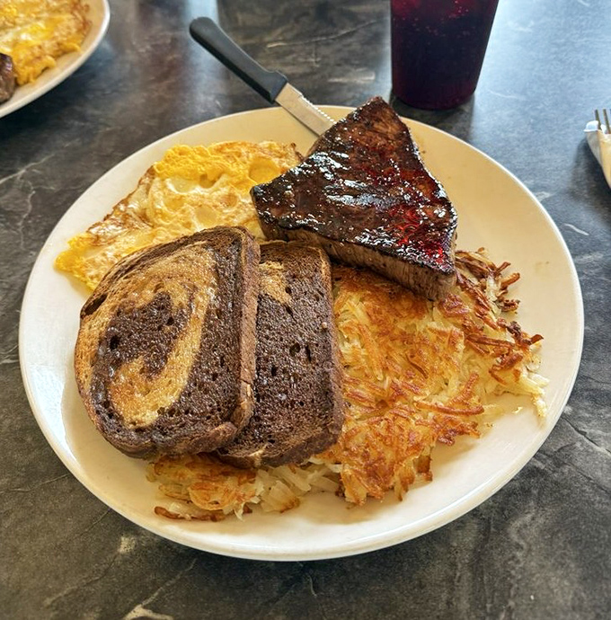 Breakfast that would make a lumberjack weep with joy – perfectly grilled ham steak, eggs, and hash browns crispy enough to make satisfying ASMR sounds.