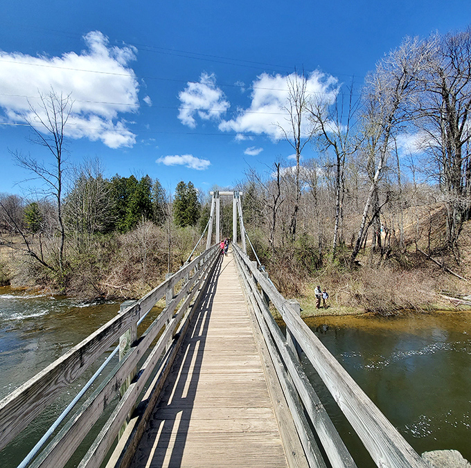 Tiny figures on a wooden ribbon, these travelers gain perspective as they cross high above the water, momentarily suspended between earth and sky.