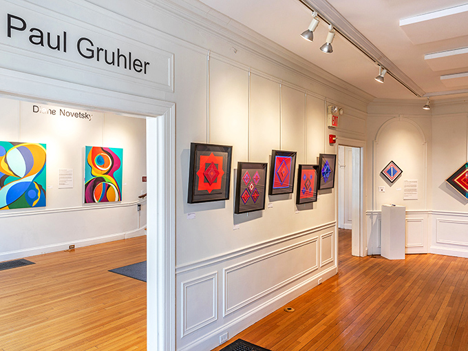 Clean white walls and warm wooden floors create the perfect gallery setting where colorful artwork pops with vibrant energy.