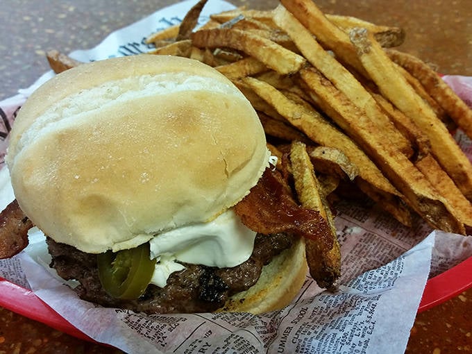 A classic burger nestled beside hand-cut fries on newspaper &ndash; simplicity perfected, with a pickle for that essential tang.