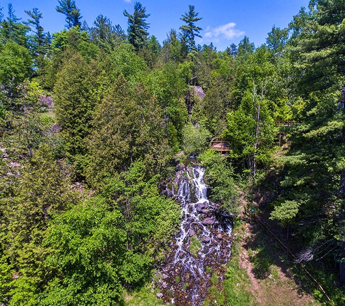 Fumee Falls cascades gently down a rocky hillside, surrounded by lush greenery that frames this accessible roadside attraction.