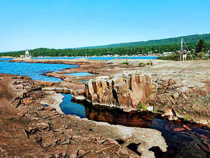 Grand Marais' picturesque harbor features rocky outcroppings that create natural pools, with the town's colorful buildings visible along the shoreline.