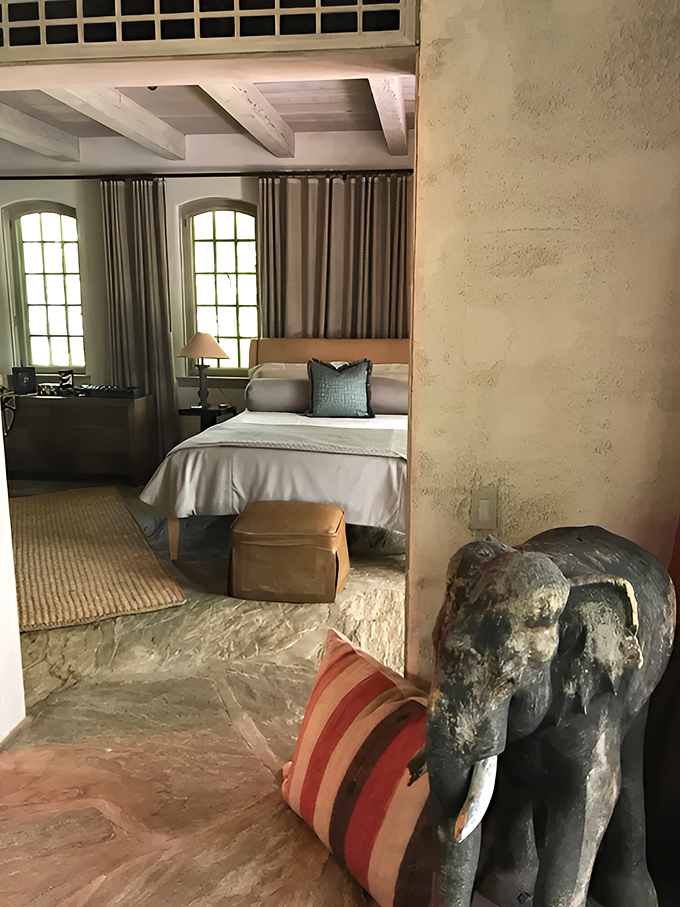 This weathered elephant sculpture stands guard by the bed, a silent storyteller of distant adventures and exotic inspirations.