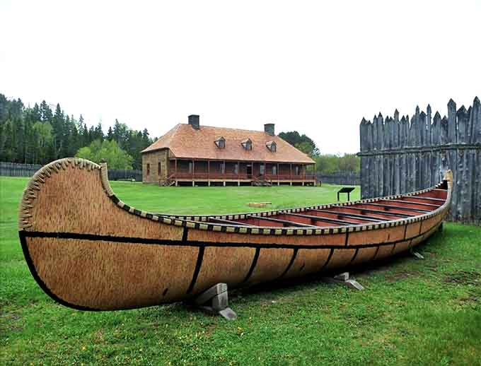 A meticulously crafted birchbark canoe rests before the historic trading post&mdash;the workhorse vessel that made the fur trade possible across impossible terrain.