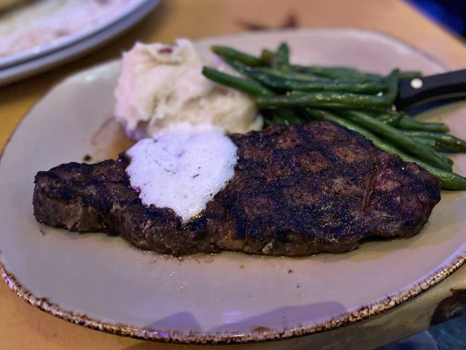 The New York Strip Steak arrives perfectly seared with a pat of melting herb butter &ndash; proof that cooking techniques have evolved nicely since the Stone Age.